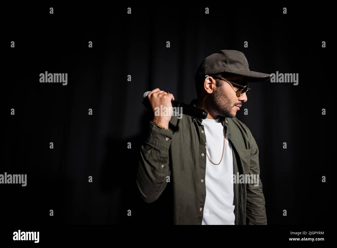 middle east hip hop performer in sunglasses holding microphone on black ...