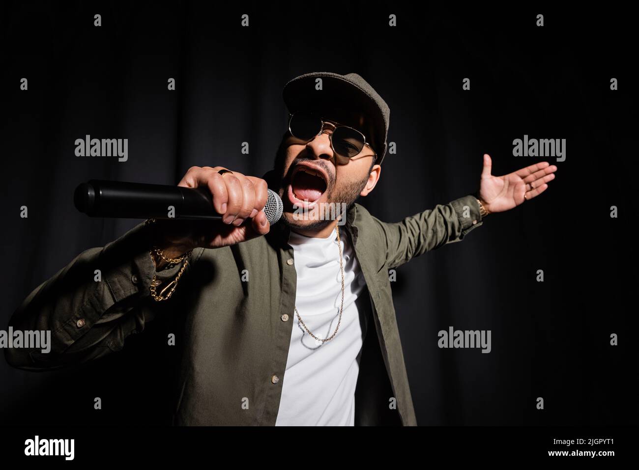 emotional eastern hip hop performer in sunglasses singing in microphone ...