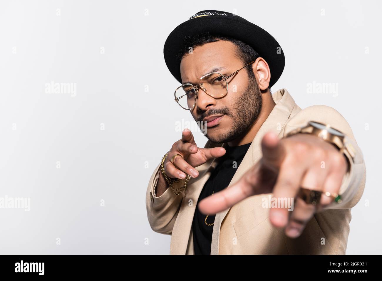 stylish indian hip hop performer in fedora hat and eyeglasses pointing ...