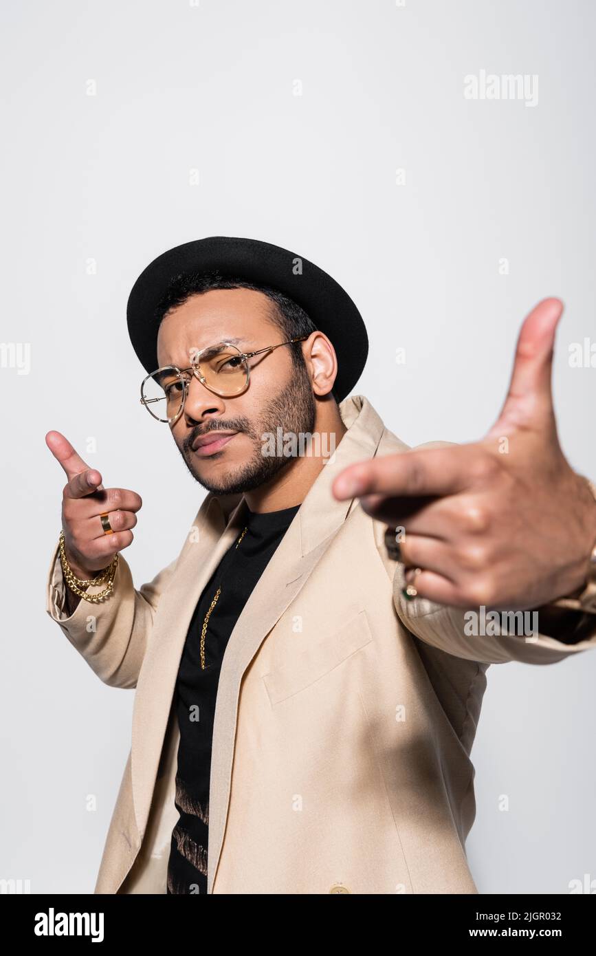 stylish indian hip hop singer in hat and eyeglasses pointing at camera ...