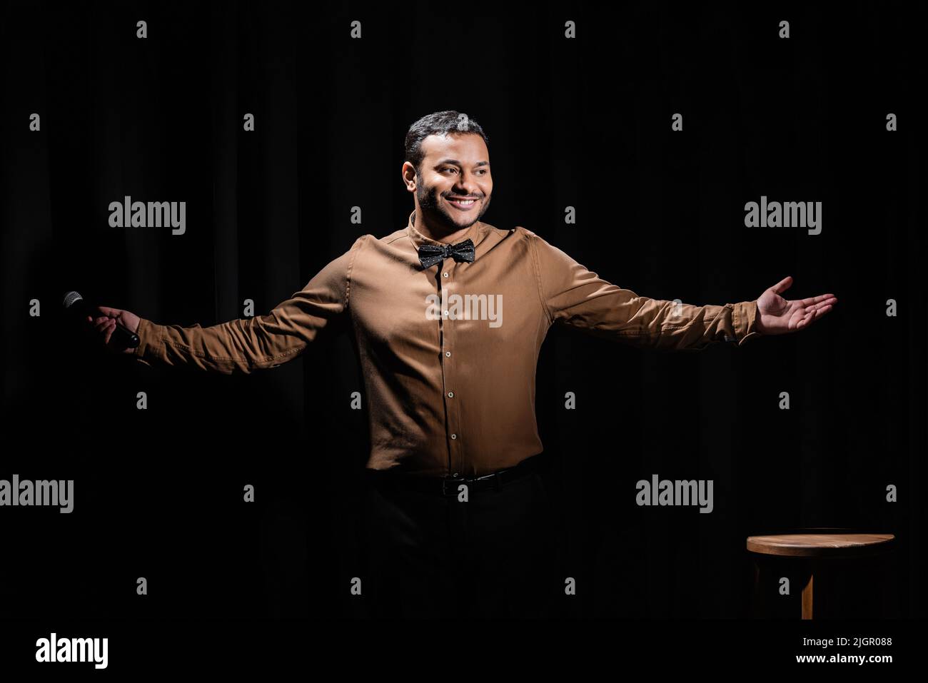 happy middle east comedian gesturing and holding microphone on black ...
