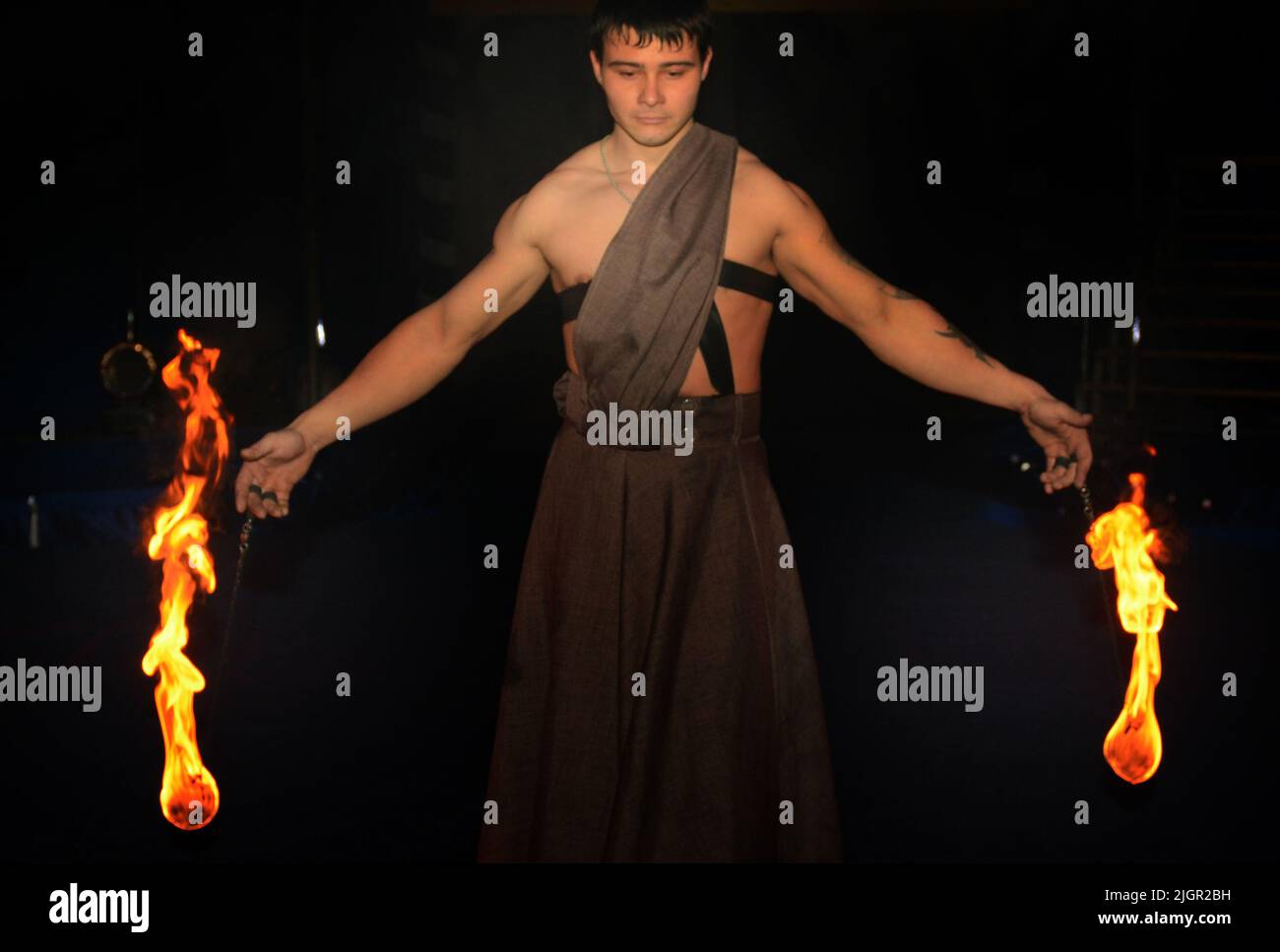 Circus fire show a man stands with fire, he is half-dressed against a ...