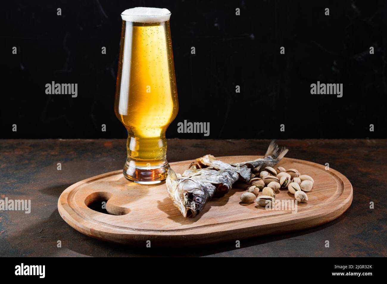 Amber beer in a narrow ale glass. Beer snack and foamy beer. Dried fish ...