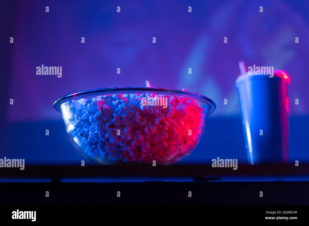 Popcorn in a glass bowl and a drink in a plastic cup on the table. Neon ...