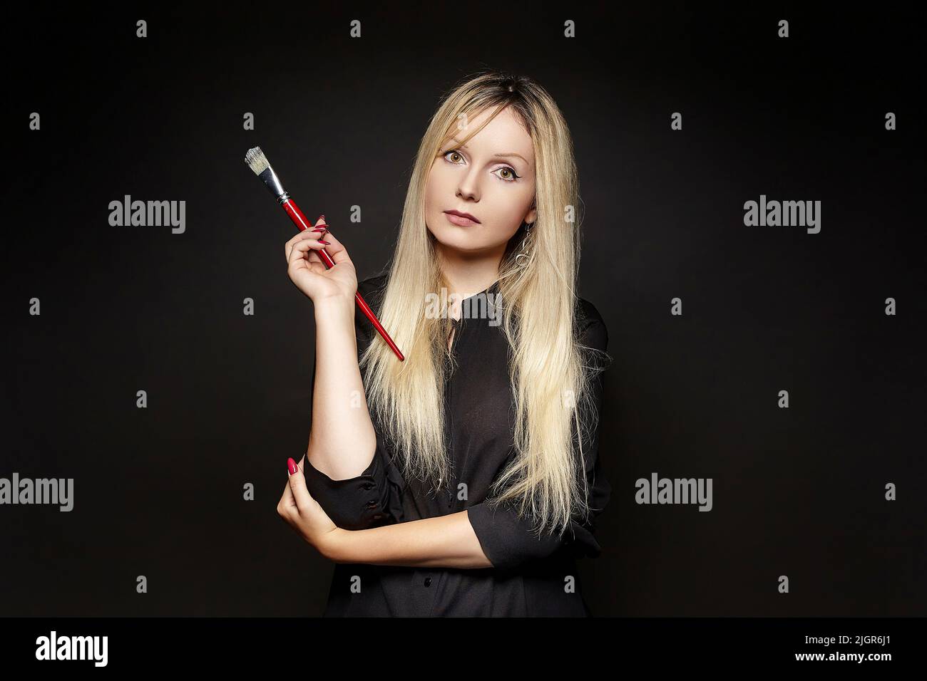 young blonde artist poses with a brush in her hand. photo shoot on a ...