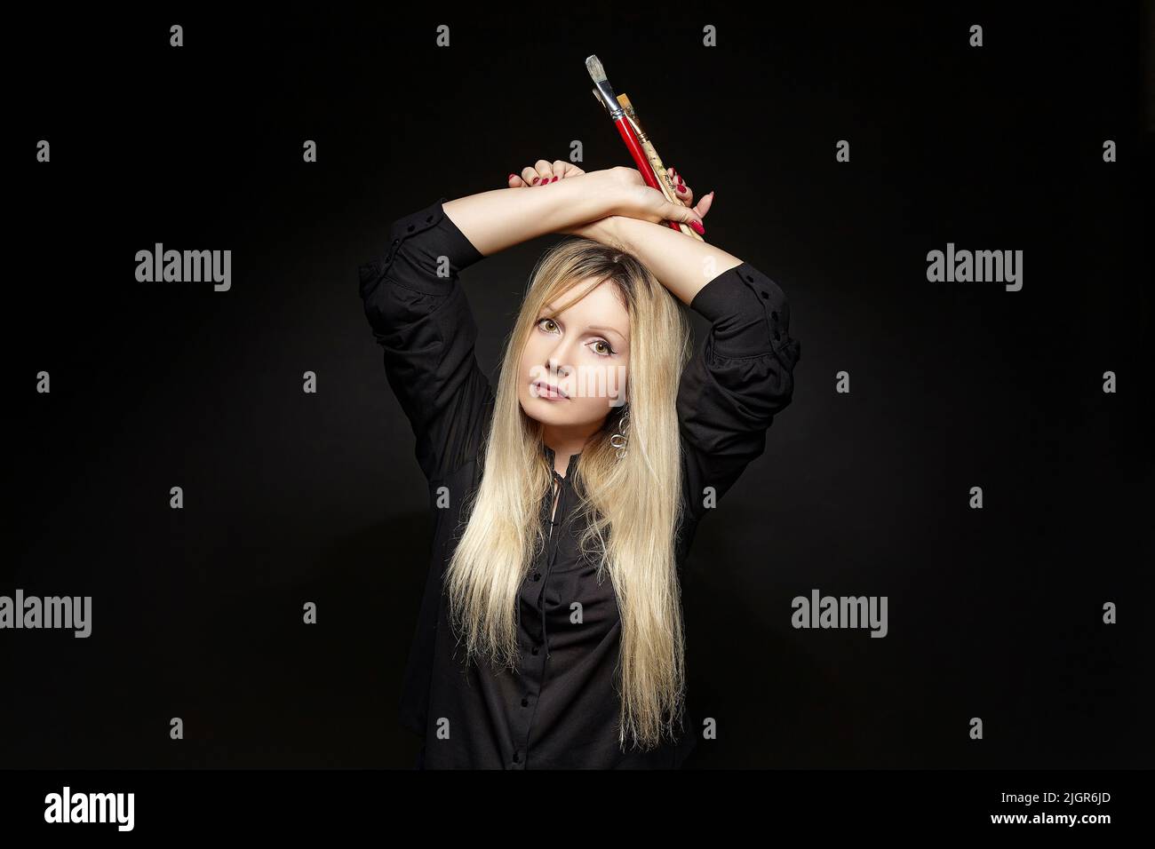young blonde artist poses with a brush in her hand. photo shoot on a ...