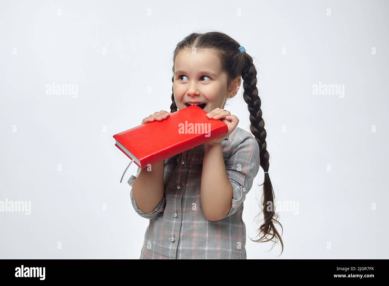 little black-haired girl holds a red book in her hands and points to ...