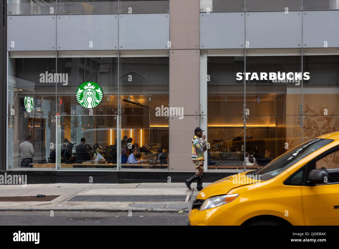 A yellow car passing by a busy Starbucks in midtown Manhattan Stock ...