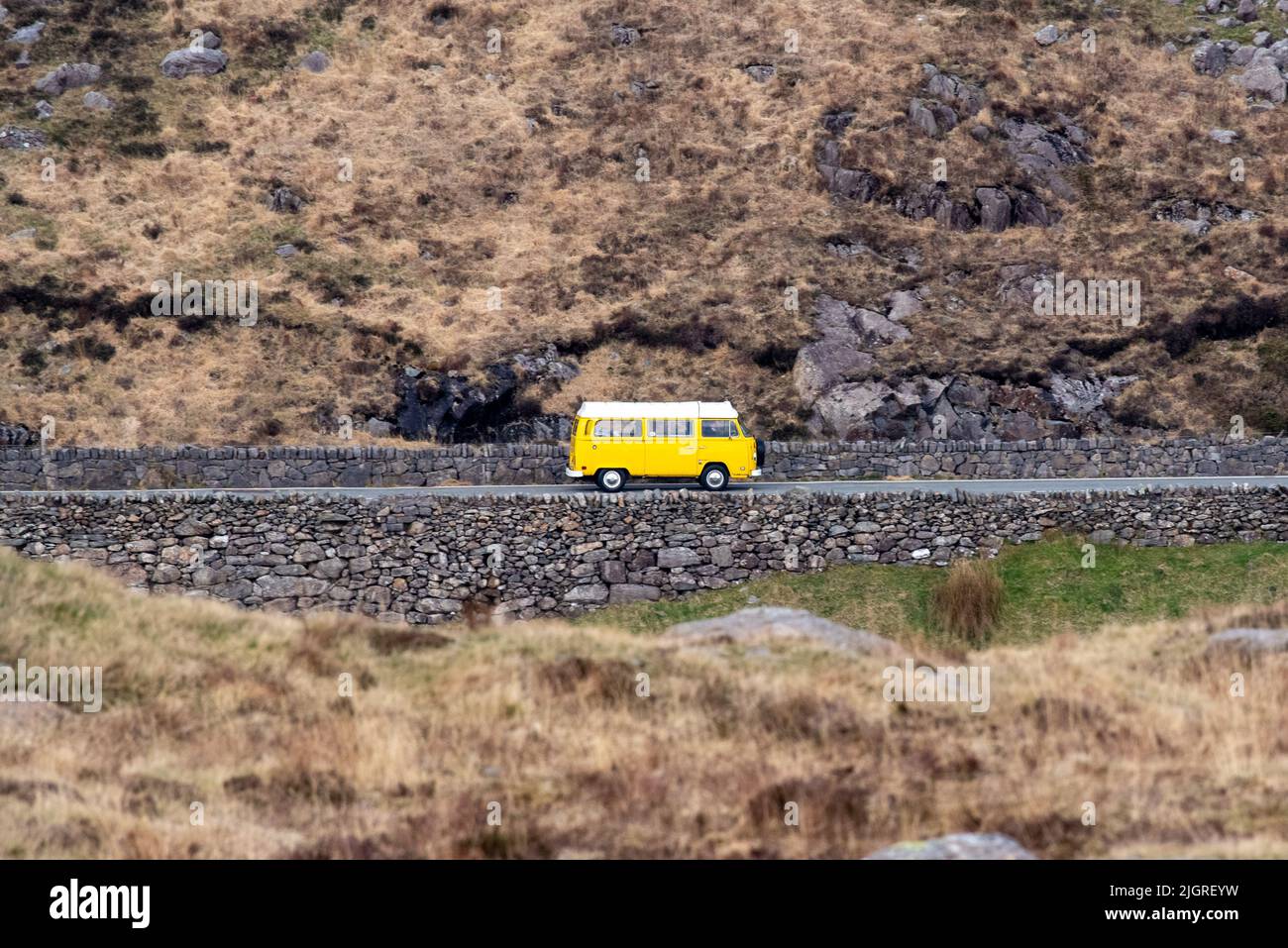 A vintage yellow van traveling on a rock-walled road in the countryside ...