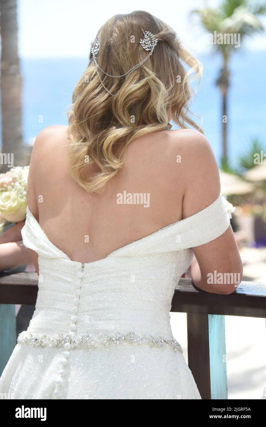 A vertical back view of a beautiful bride looking at the beach in a ...
