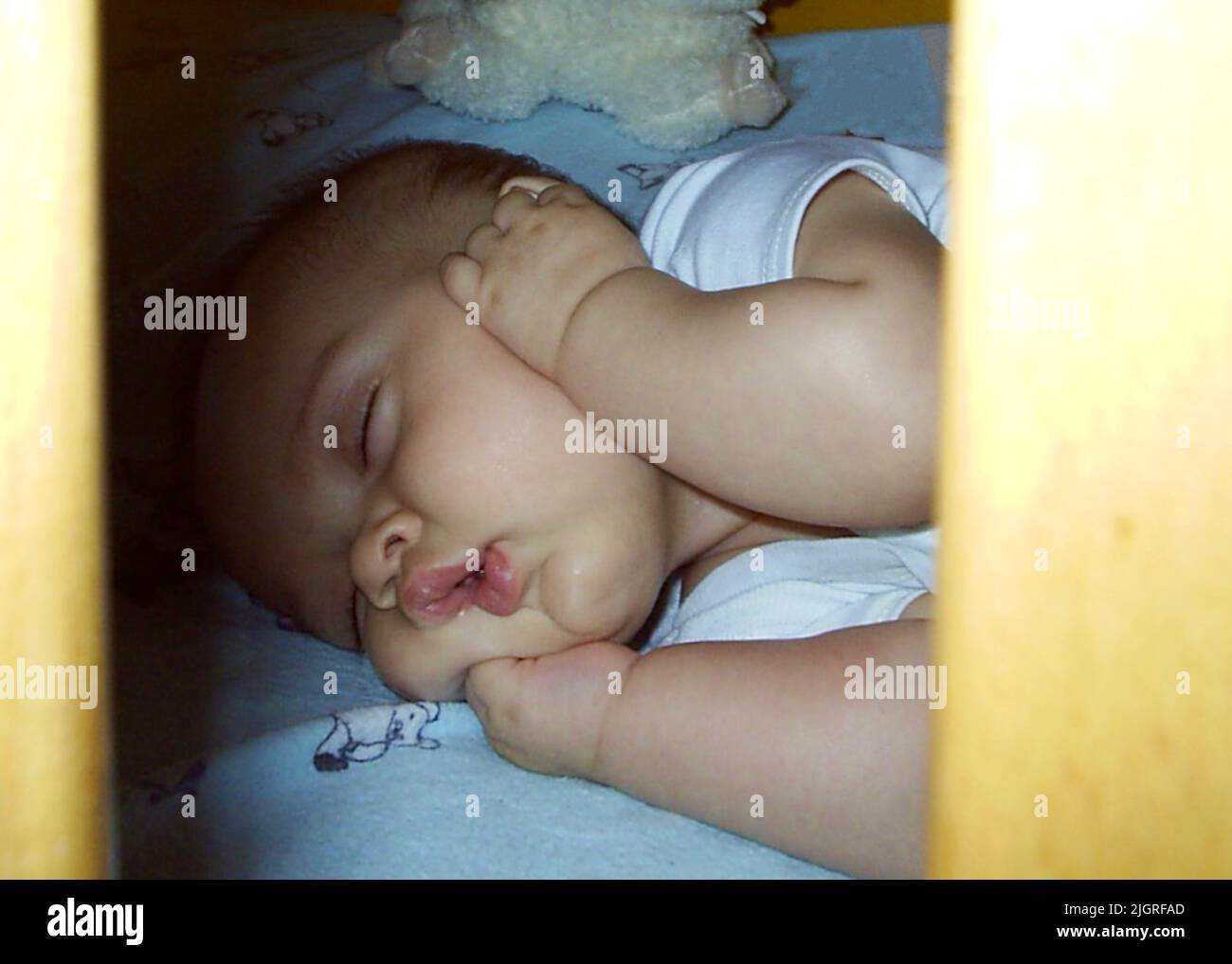 Cute baby with hands on cheeks and pursed lips sleeps in crib. Photo ...