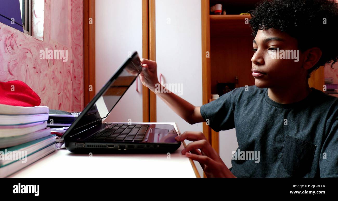 Child sitting down at desk opens laptop and turns computer on preparing ...