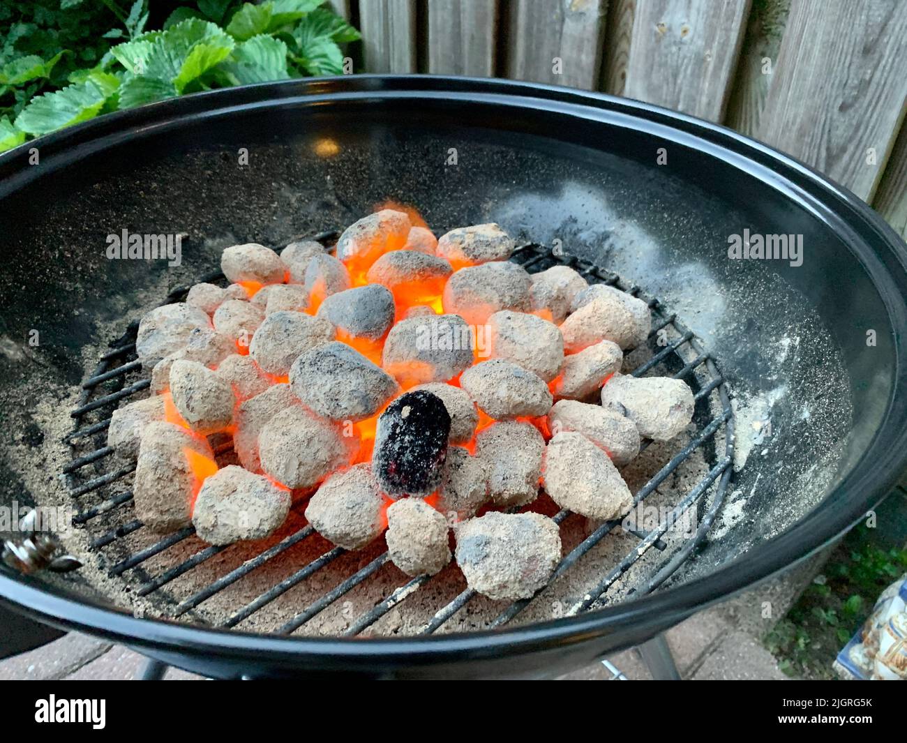 A shot of lit hot coal briquettes on the grill with one black coal on ...