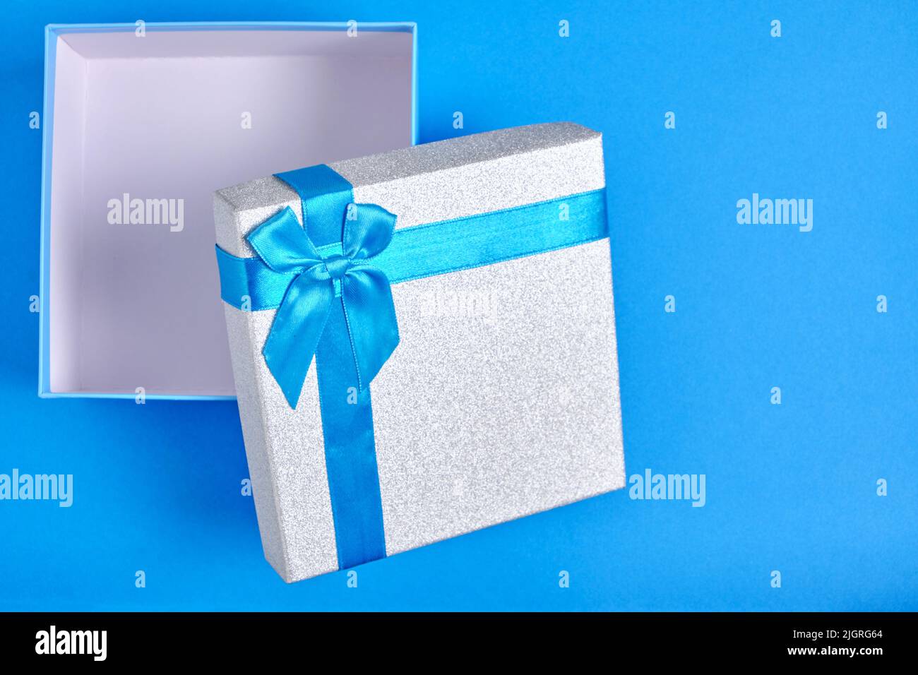Open gift box with blue ribbon and bow blue background Stock Photo - Alamy