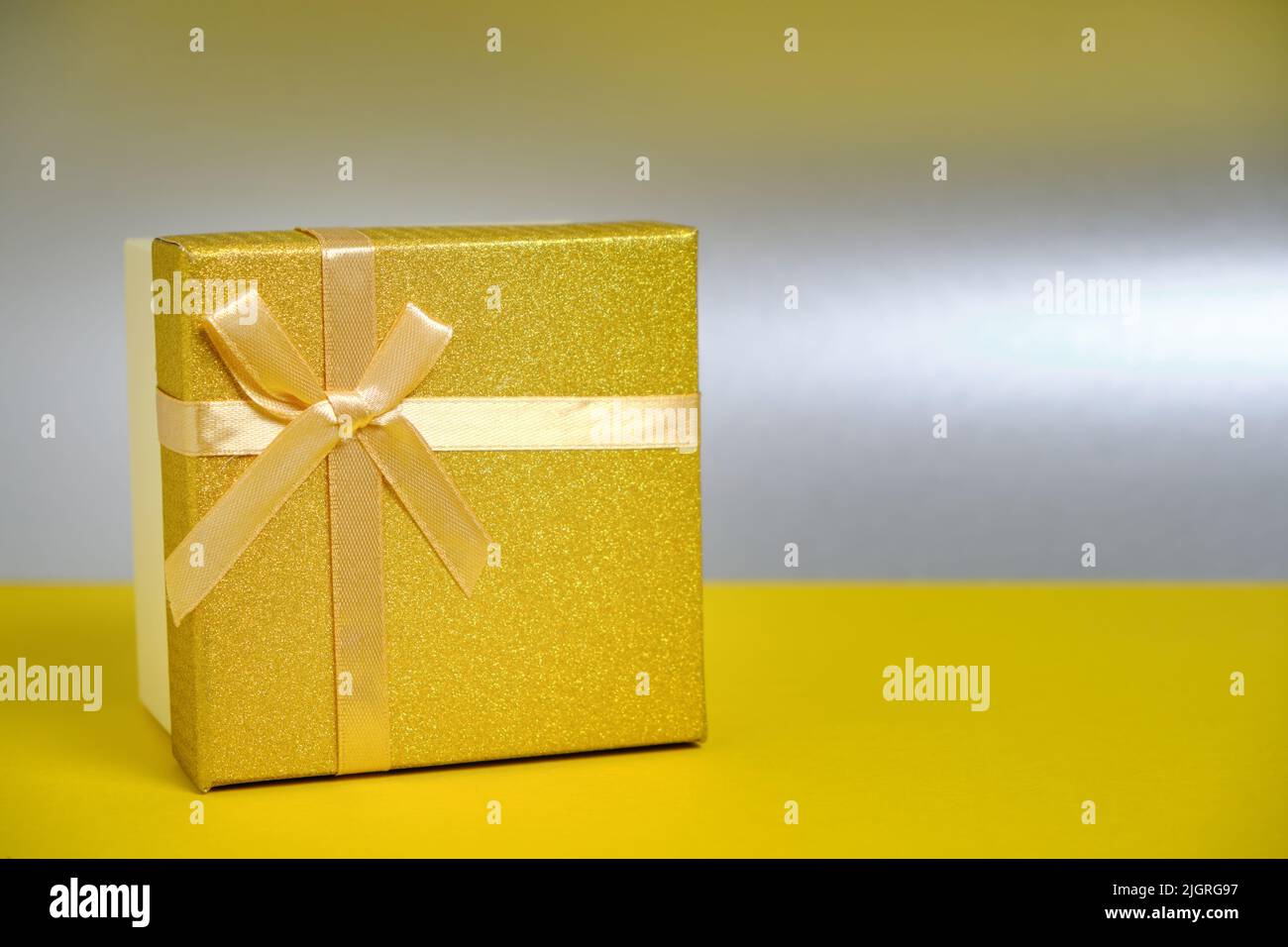 Golden gift box is tied with ribbon with bow silver background Stock ...