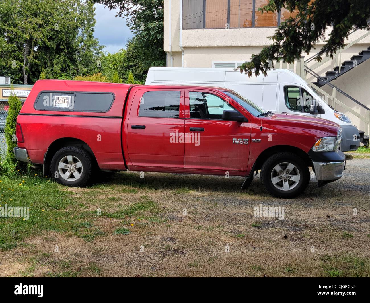 A red Ram 1500 truck parked in the yard of a house with a sprinter in ...