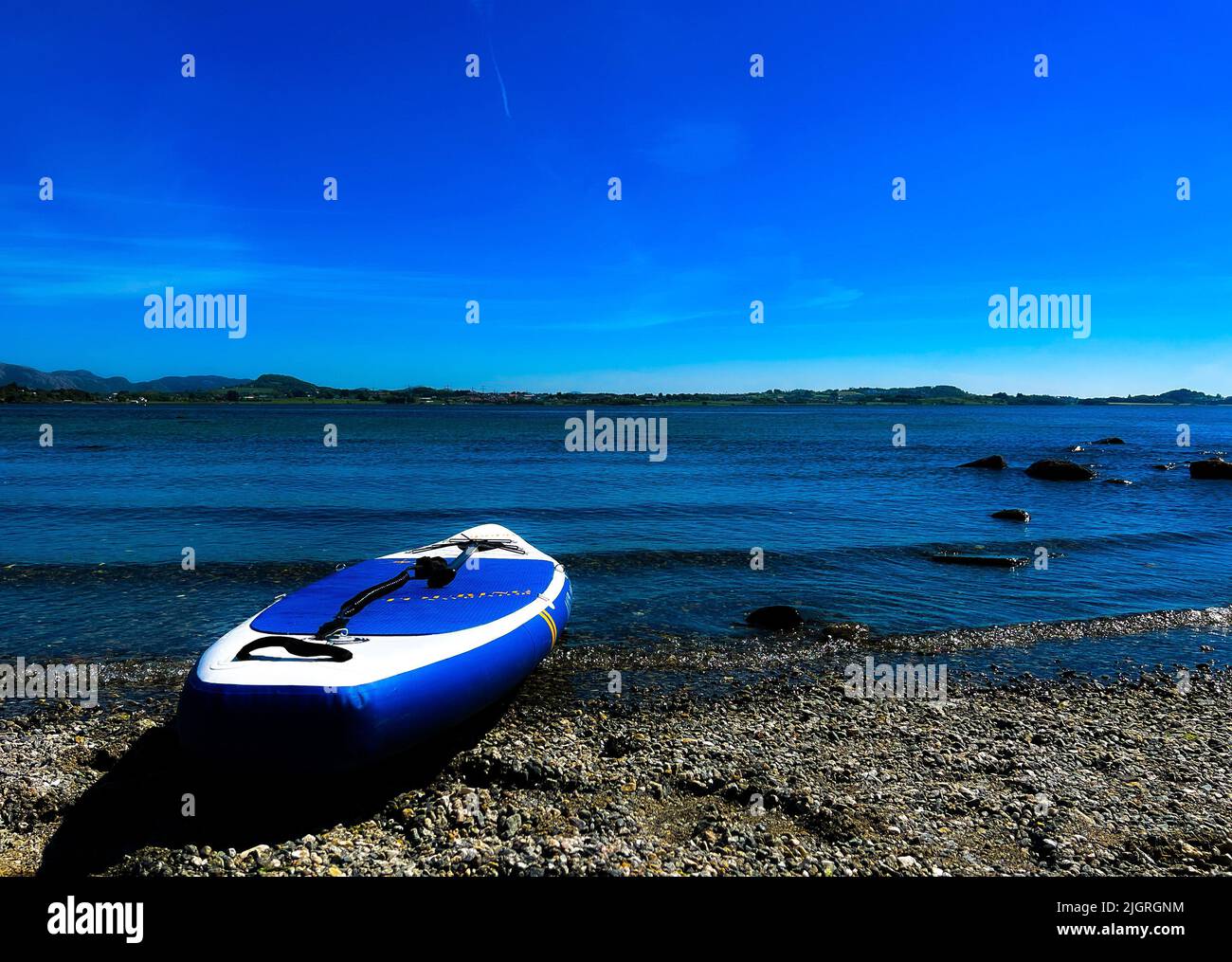 A blue standup paddle board on the beach with the sea and clear sky in ...