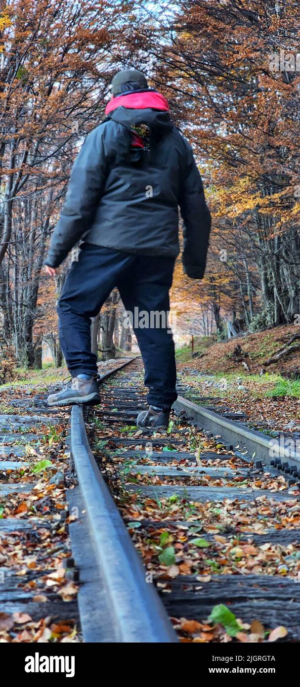 A back view of Caucasian man in warm clothes standing on train rails ...