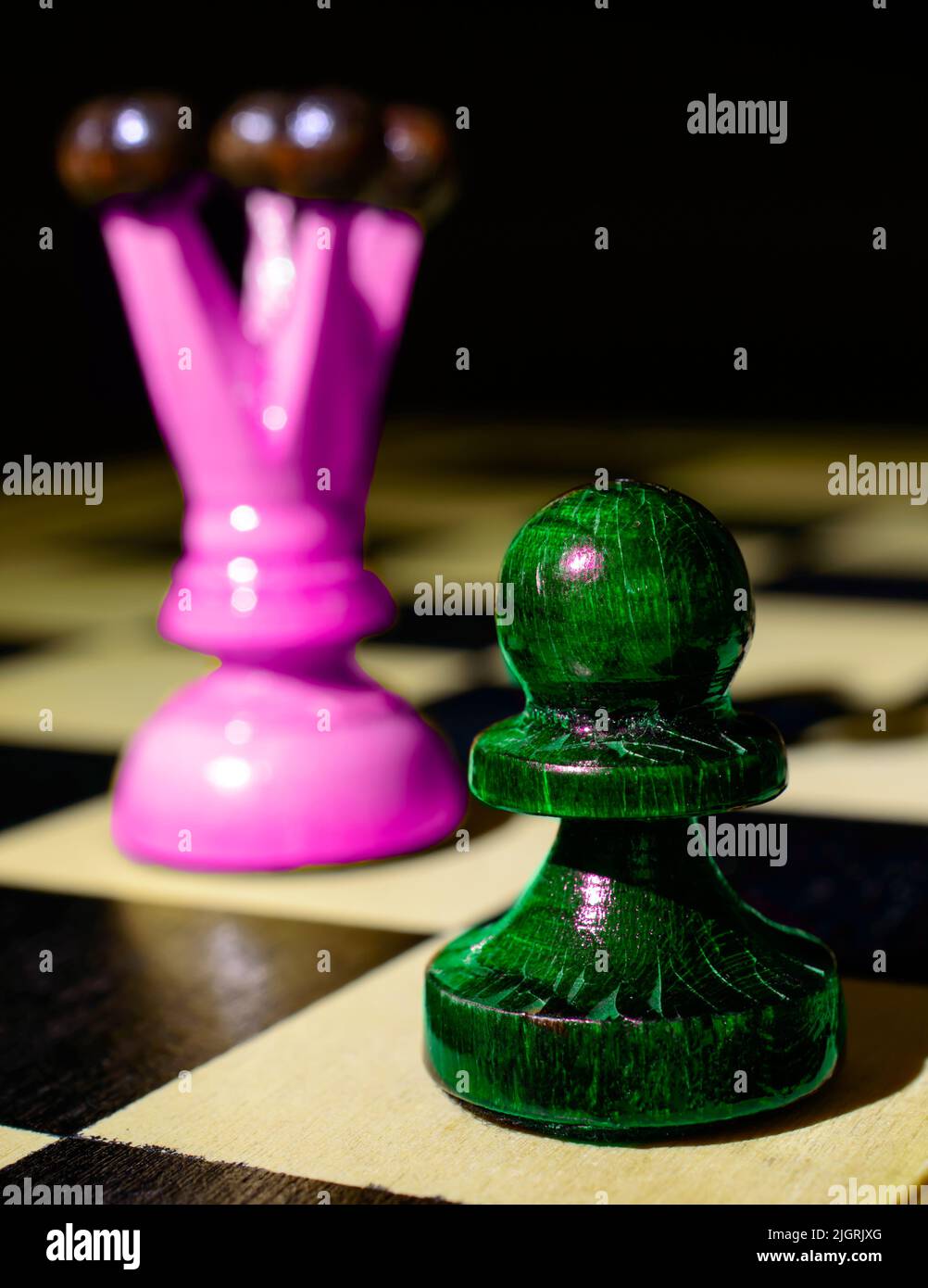 Green pawn and purple Queen on a chessboard. Dark background. Selective ...