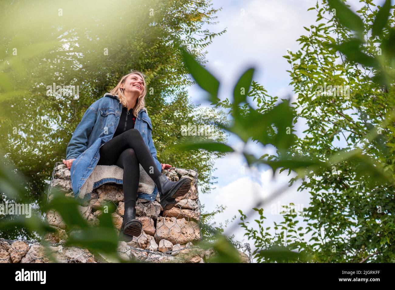 Happy stylish girl sitting on a rock in the middle of the green nature ...