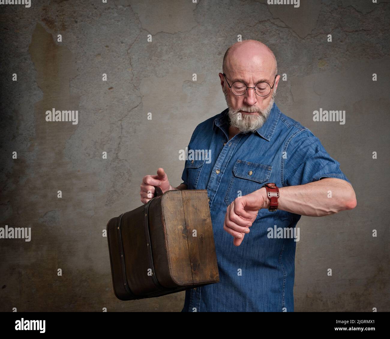 checking time - a senior man with a retro suitcase is looking at his ...