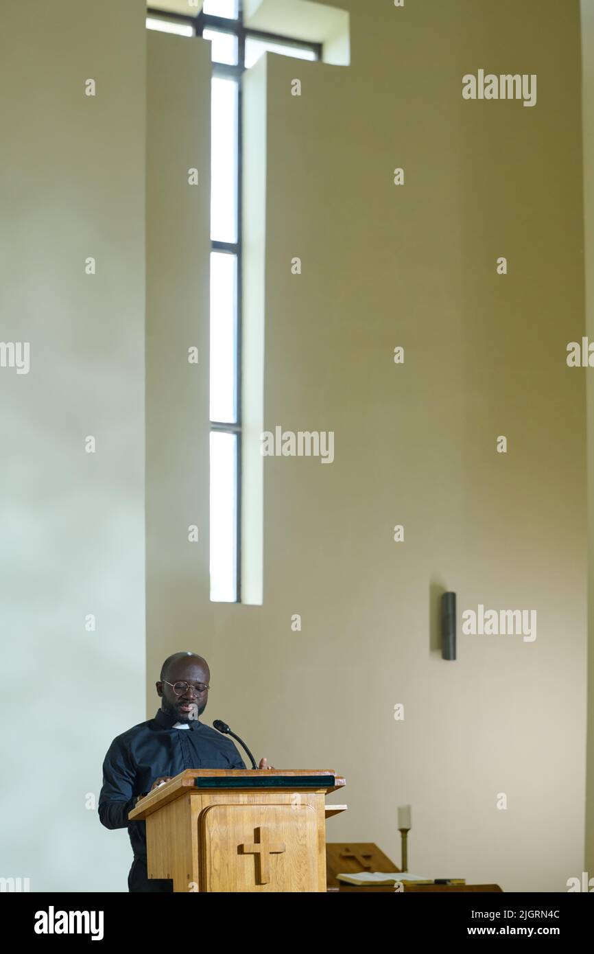 Young black man standing by wooden pulpit in front of parishioners ...