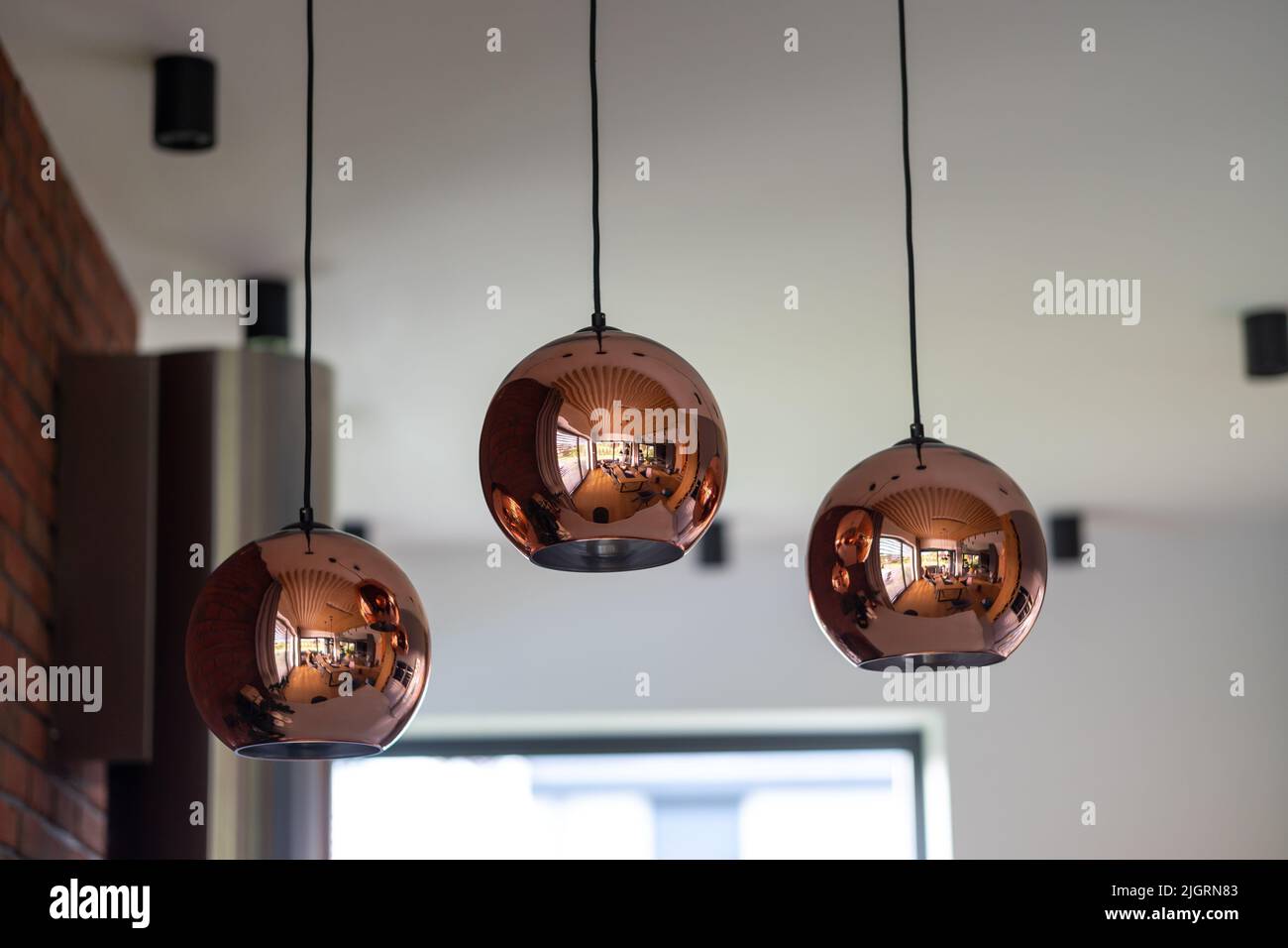 A close-up shot of three shiny bronze lamps hanging from the ceiling ...