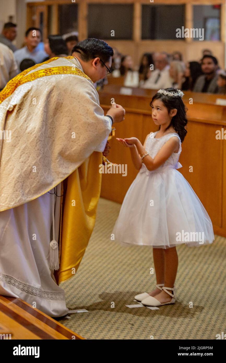 A gowned Vietnamese American priest offers a communion wafer to a ...