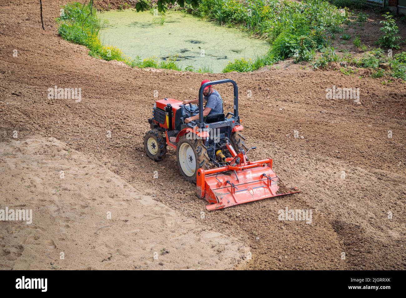 A farmer on a mini tractor loosens the soil for the lawn. Land ...