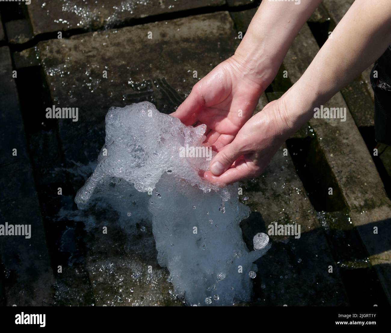 Hands touch the fountain. A stream of water from the fountain is ...