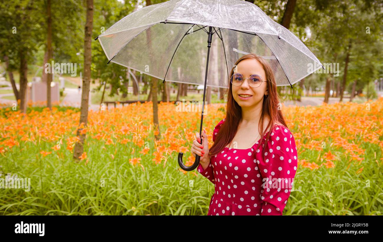 Young woman in glasses with transparent umbrella standing in rainy ...