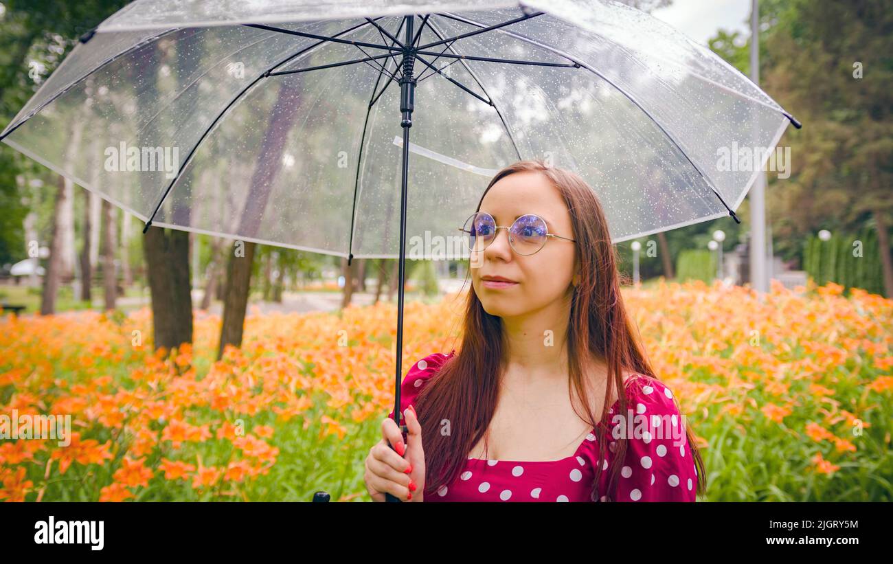 Young woman in glasses with transparent umbrella standing in rainy ...