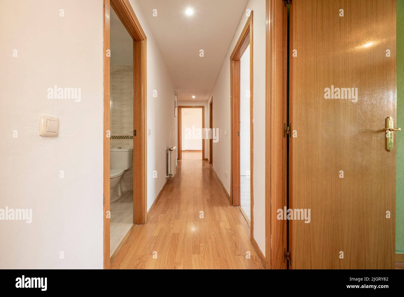 Plain white painted hallway with entry to multiple rooms and oak ...