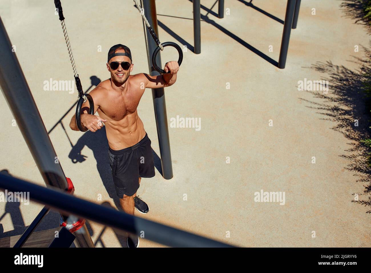 Muscular sportsman exercising on outdoor gymnastic rings in outdoor gym ...