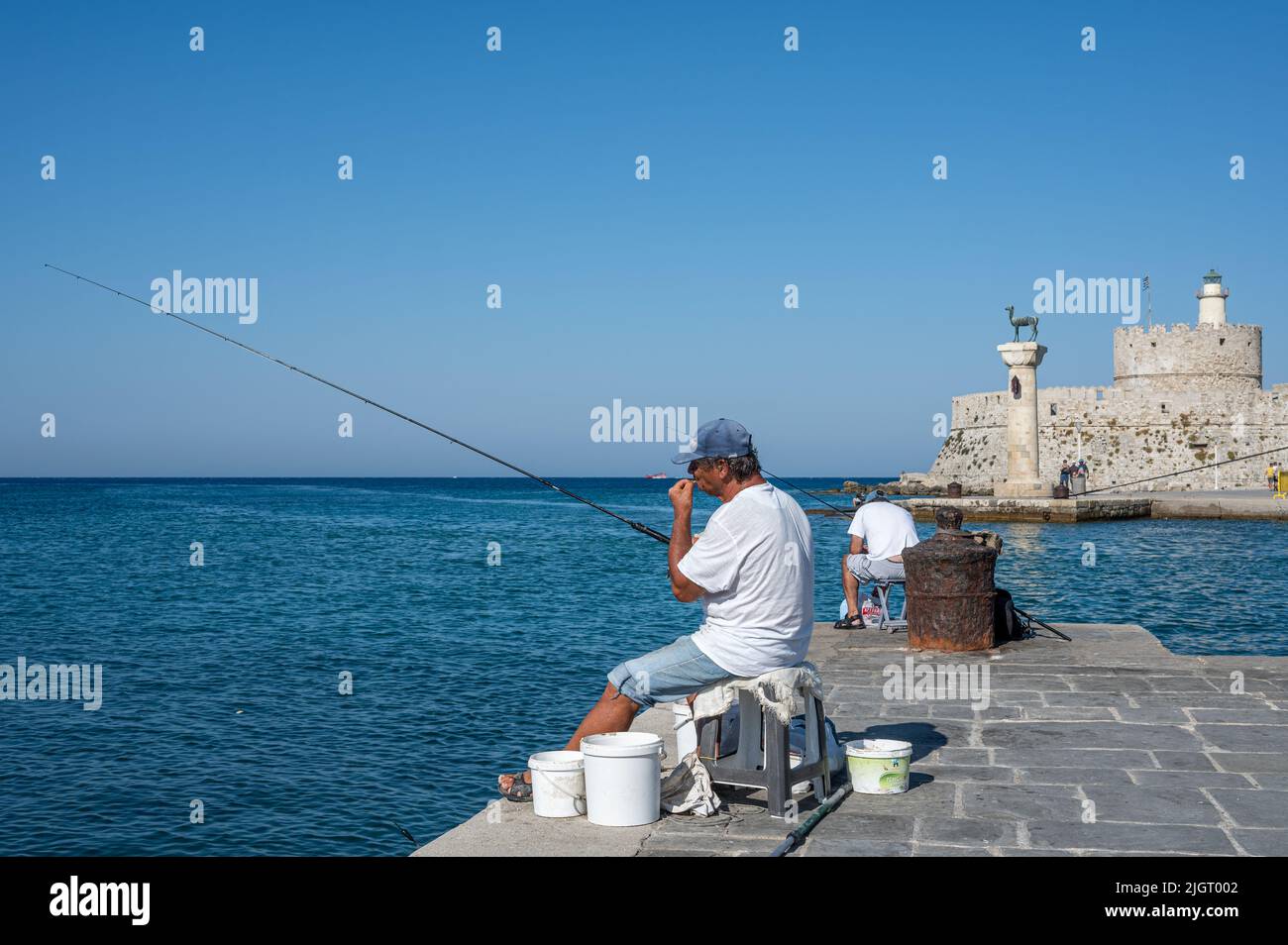 Fisherman at Mandraki harbour in front of St Nicholaos Castle in Rhodes ...