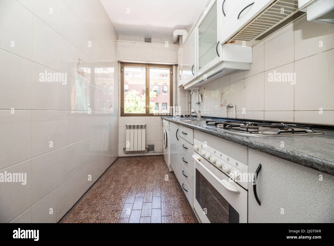 Elongated kitchen with white furniture and stone countertop and window ...