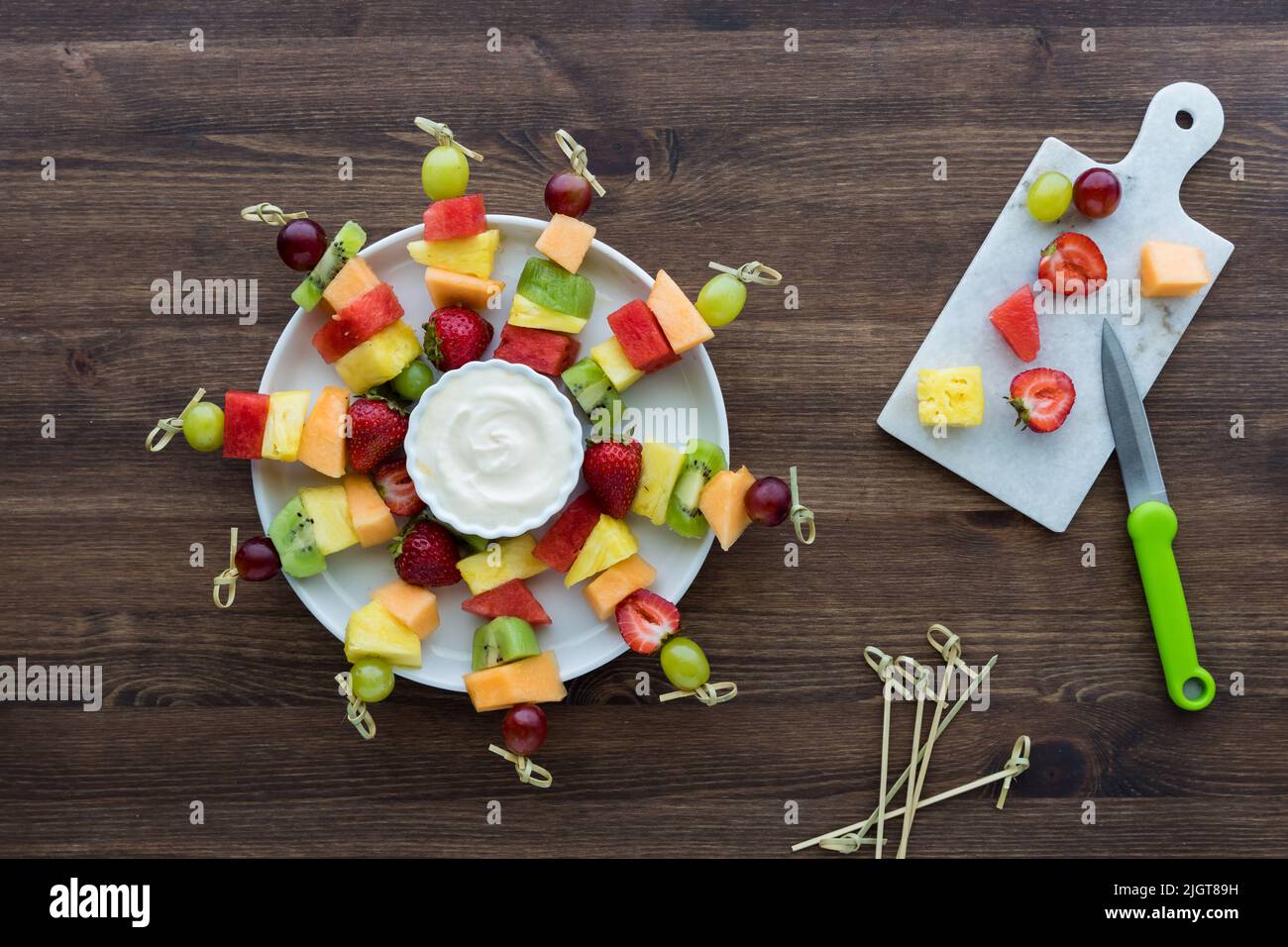 Depiction of preparing a platter of fresh fruit skewers, on a dark ...