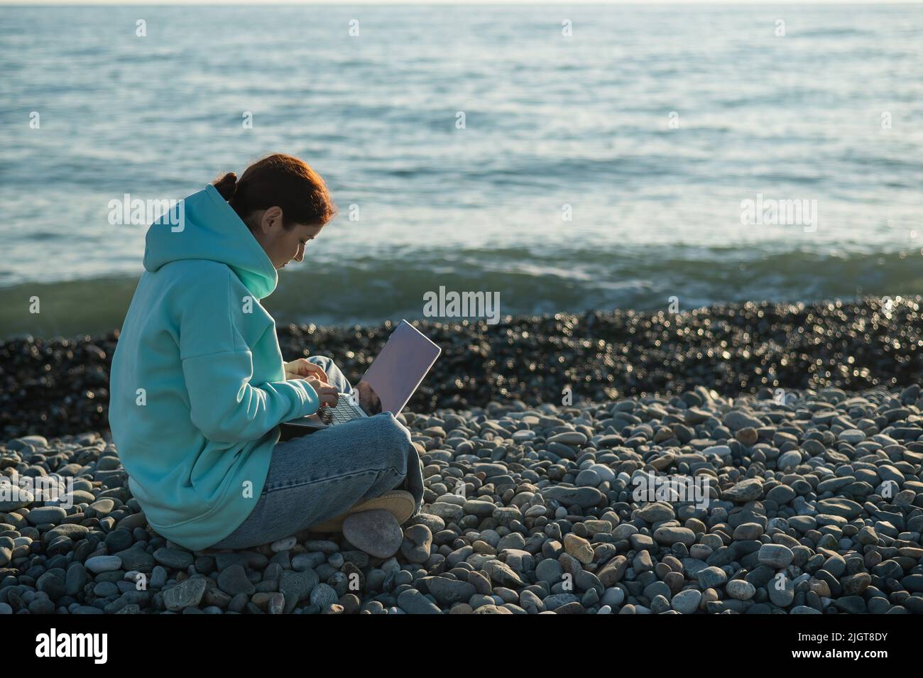 Happy caucasian woman working on a laptop while sitting on a pebble ...