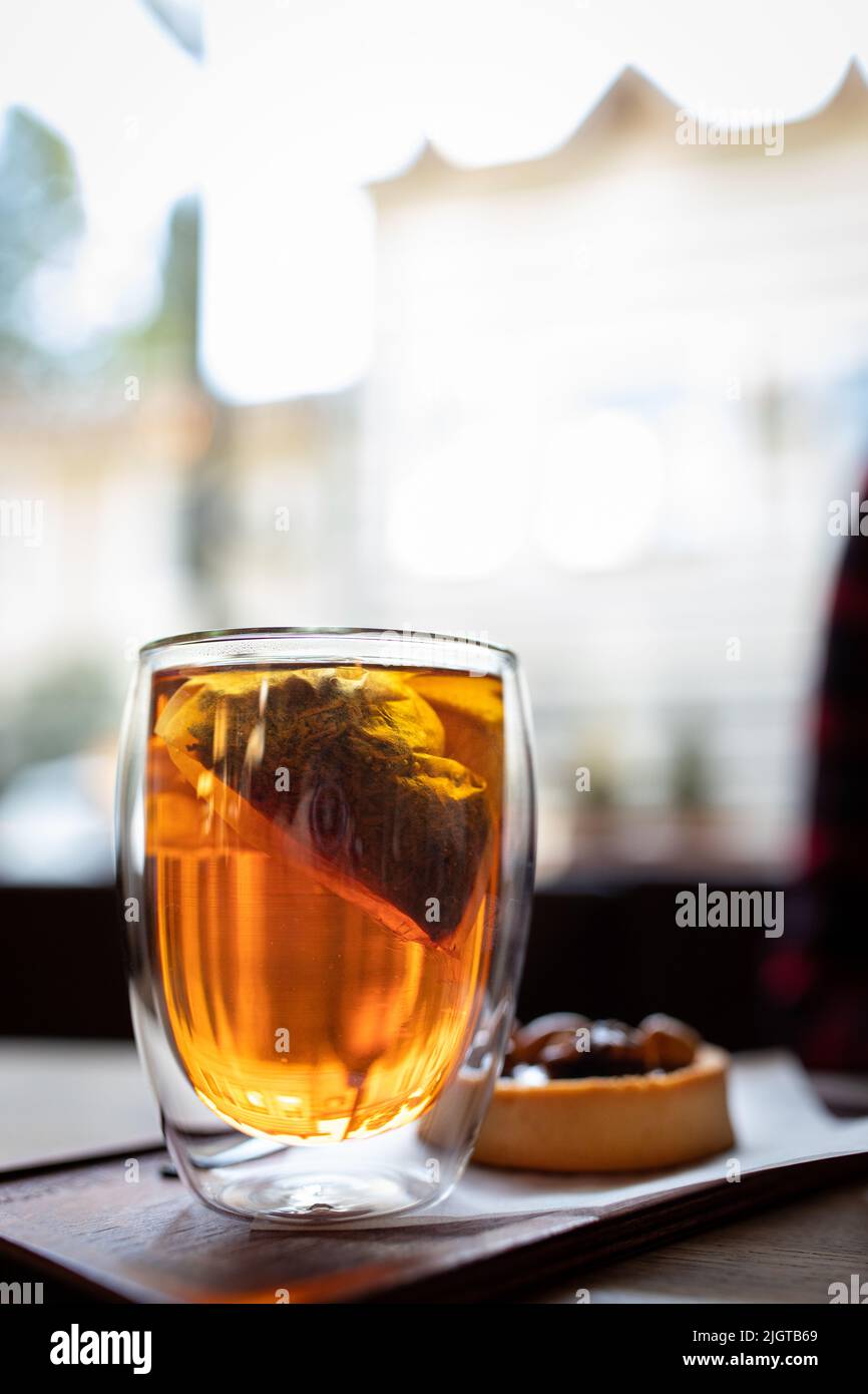A clear mug of tea with lemon and dessert on the coffee shop table ...