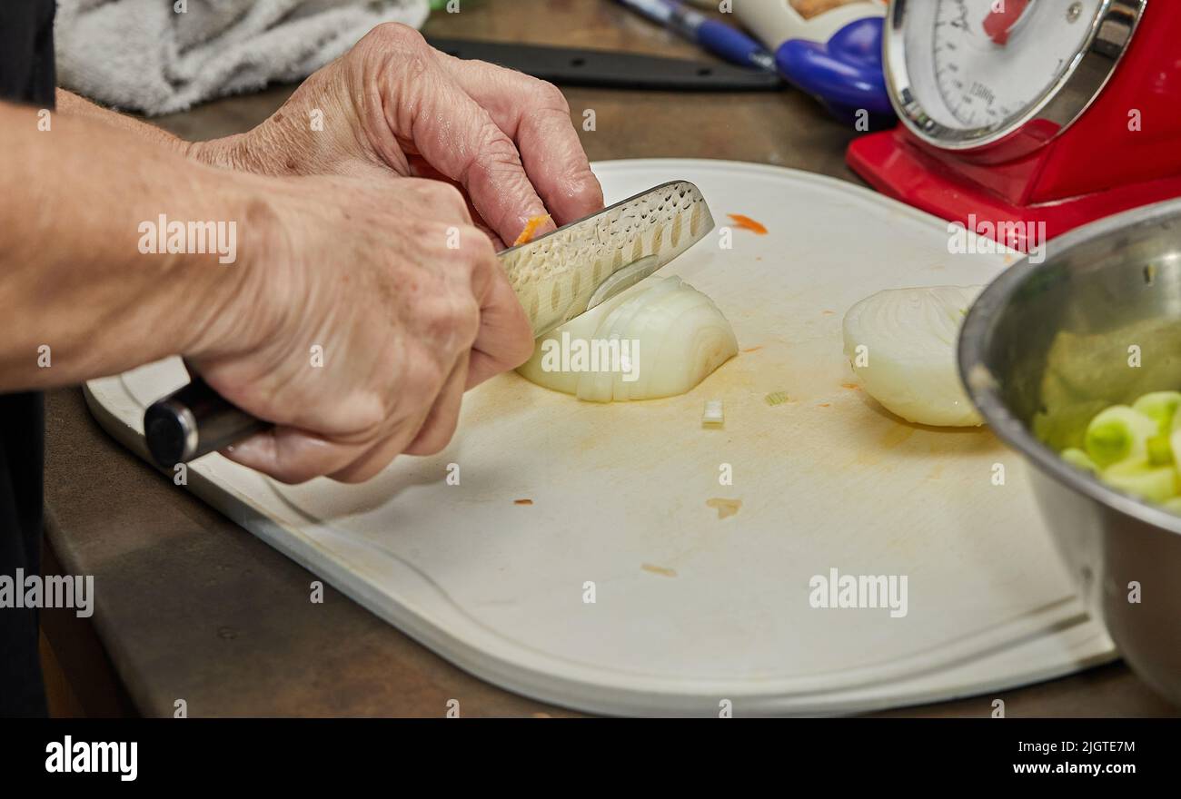 Chef cuts the onion into slices on the board in the home kitchen Stock ...