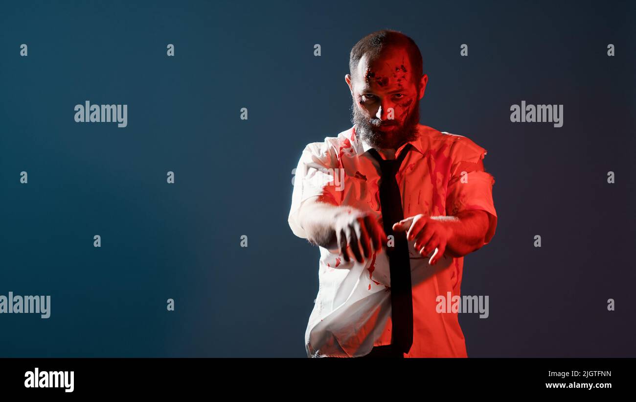 Spooky zombie growling at camera while standing on blue background ...
