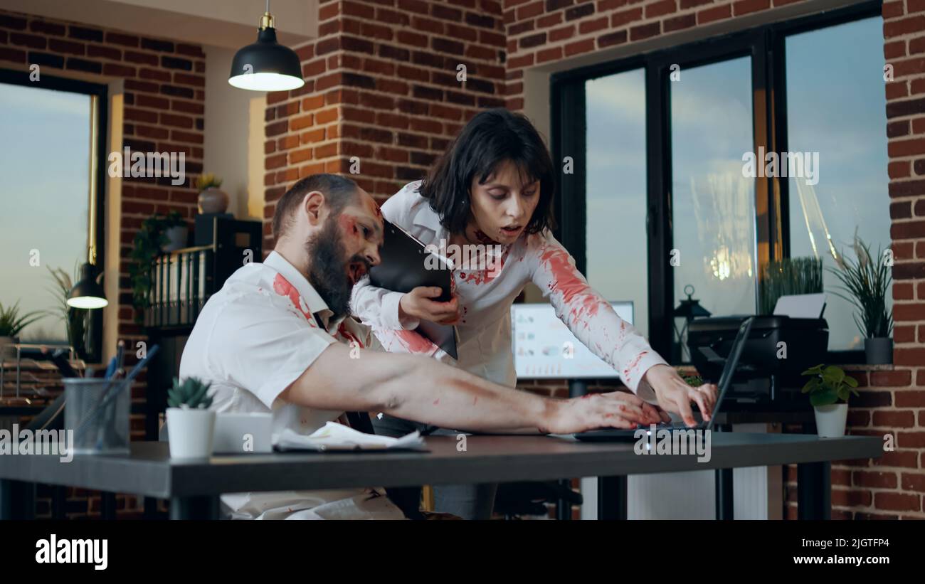Scary office zombie with bloody wounds in workspace working on modern ...