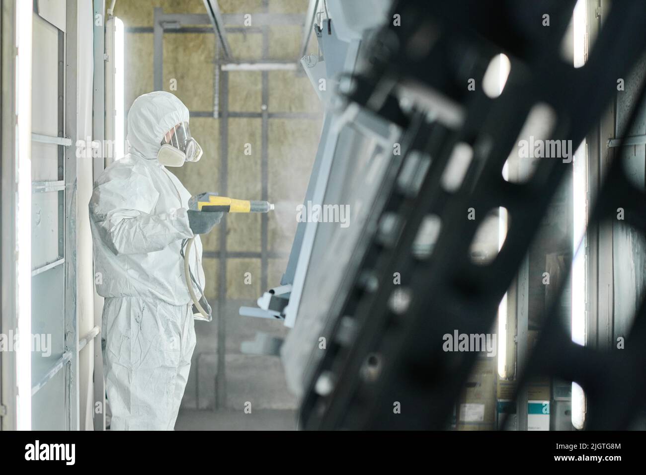 Industrial worker in protective workwear using spray gun to paint metal ...