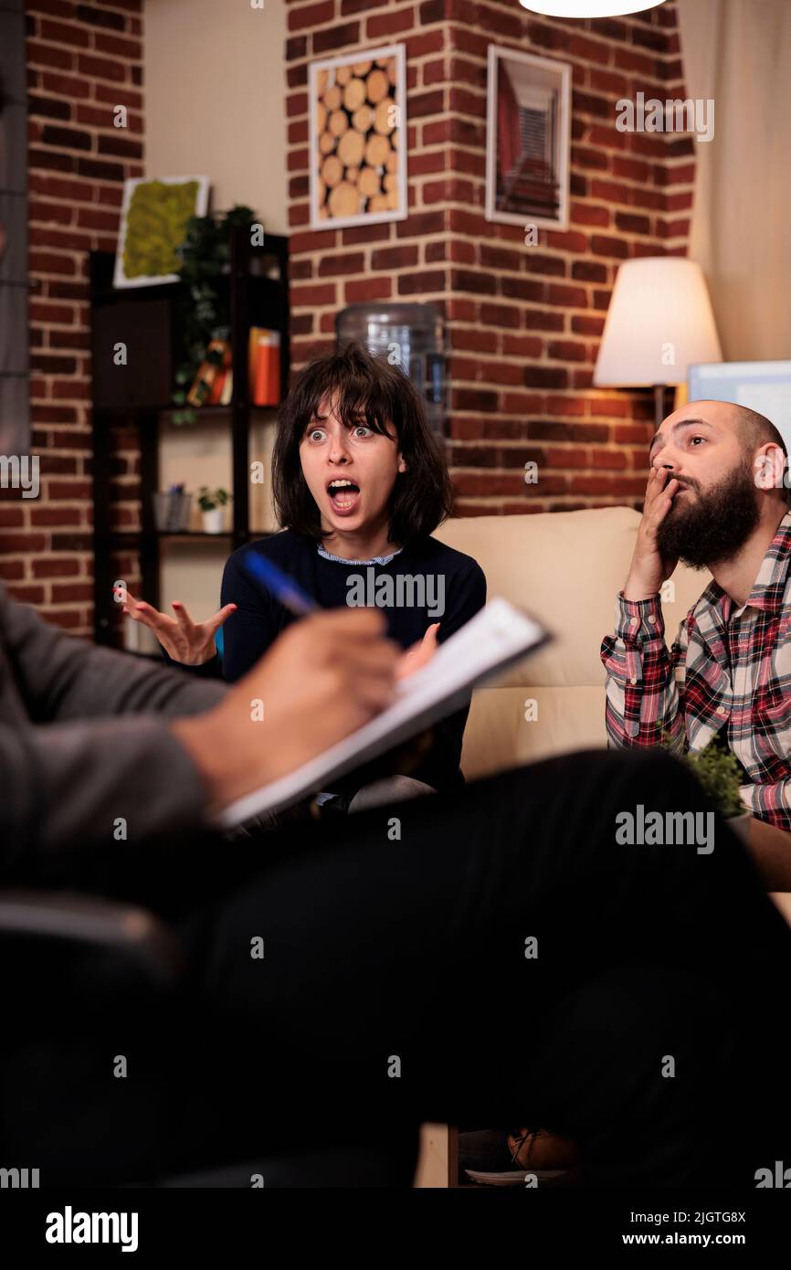 Male psychologist taking notes on paper at couple therapy with angry ...