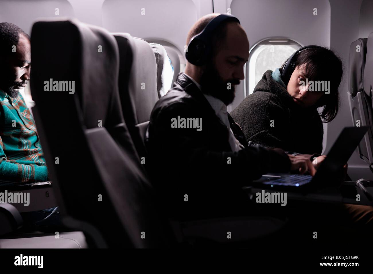 Female passenger looking at man during airplane flight, using laptop ...