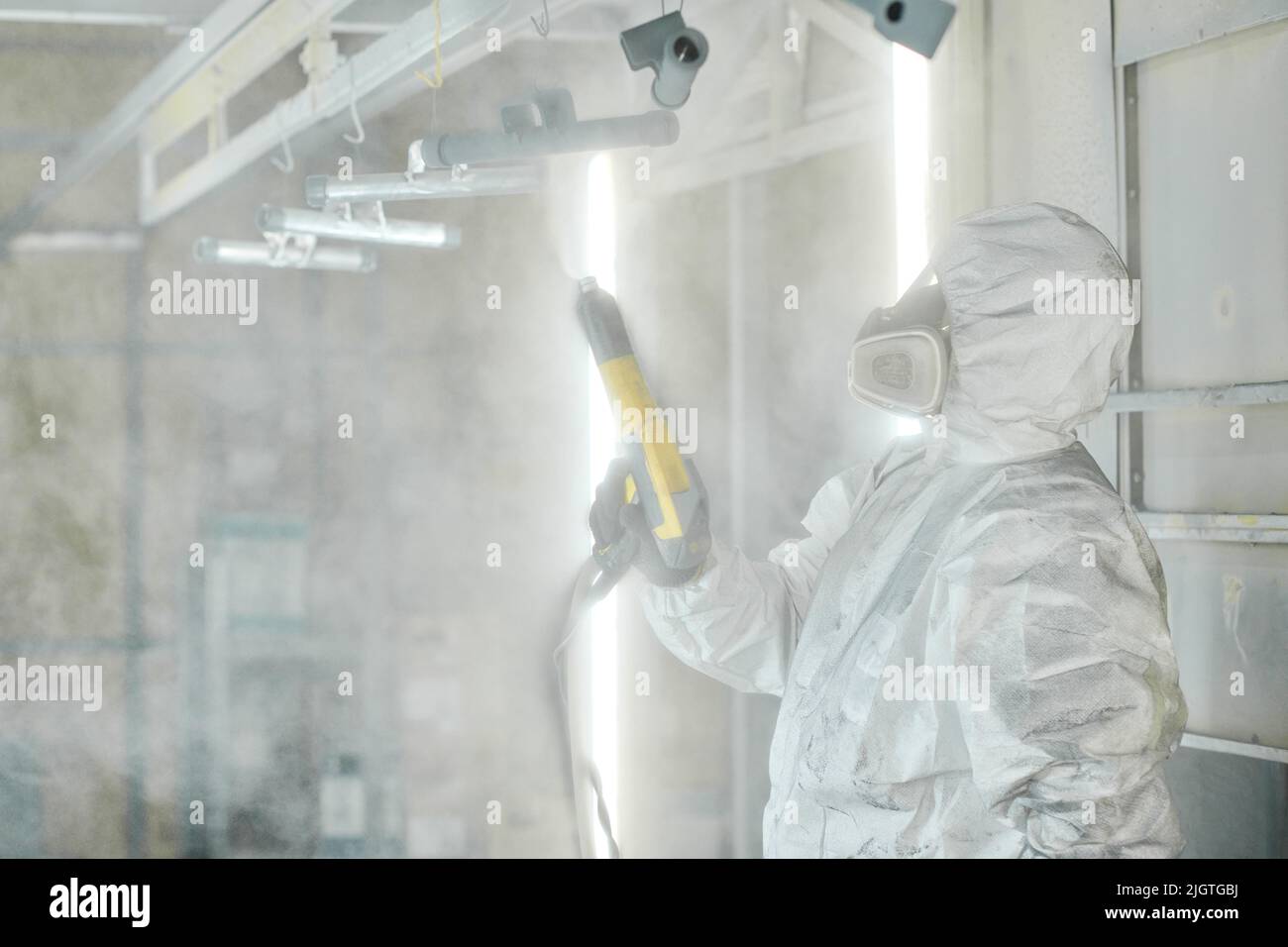 Worker in protective suit working with spray gun to paint metal details ...