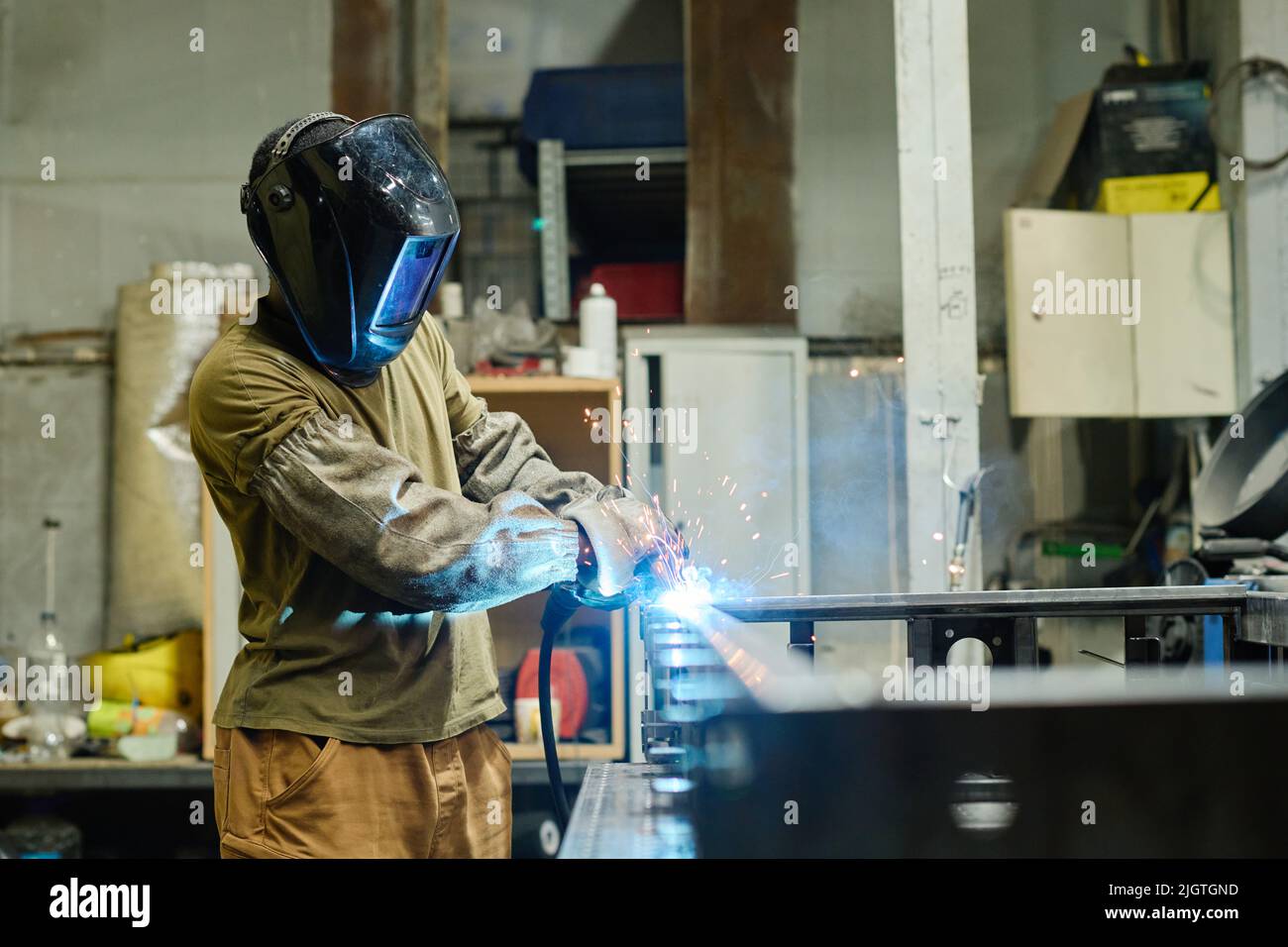 Welder in mask using torch to cut iron at his workplace in workshop ...