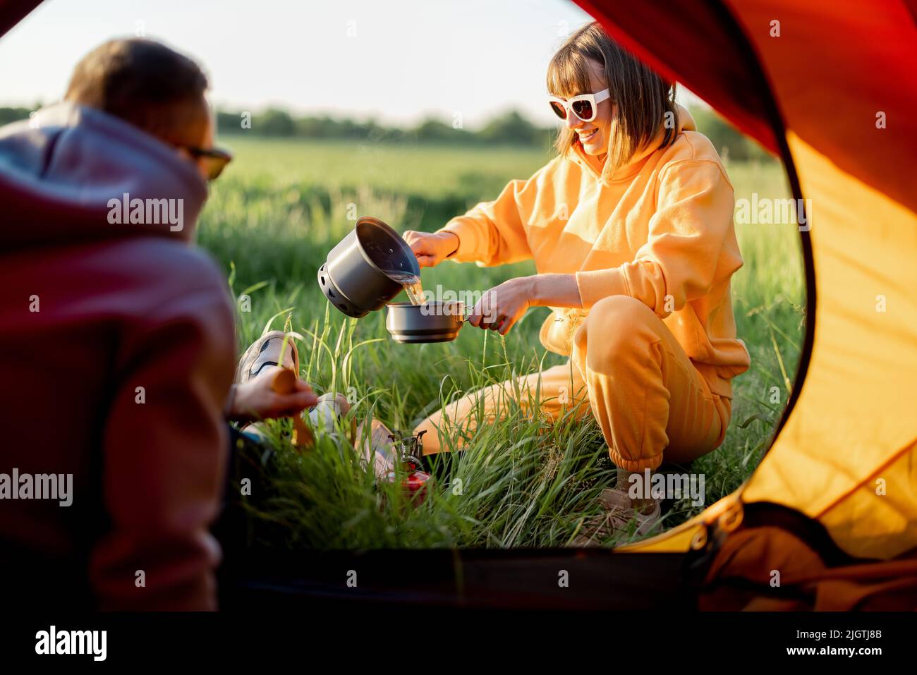 Couple prepare food while traveling with tent on nature Stock Photo - Alamy