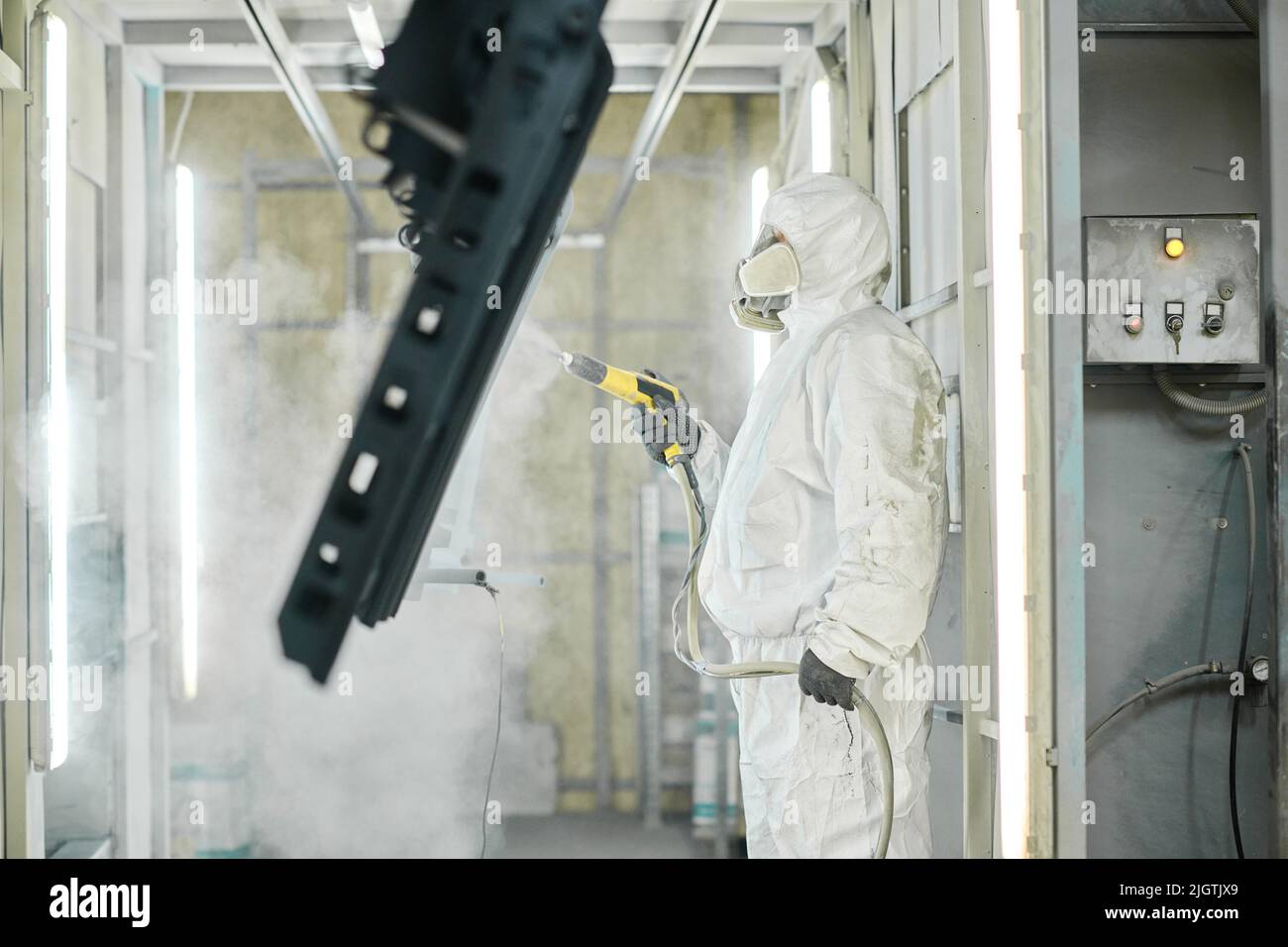 Worker in protective suit and mask using spray gun to paint steel ...