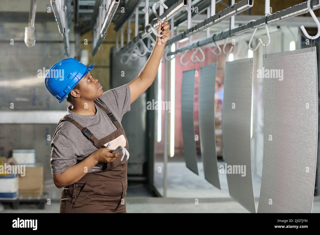 African female worker in hardhat hanging finished products on a rack ...